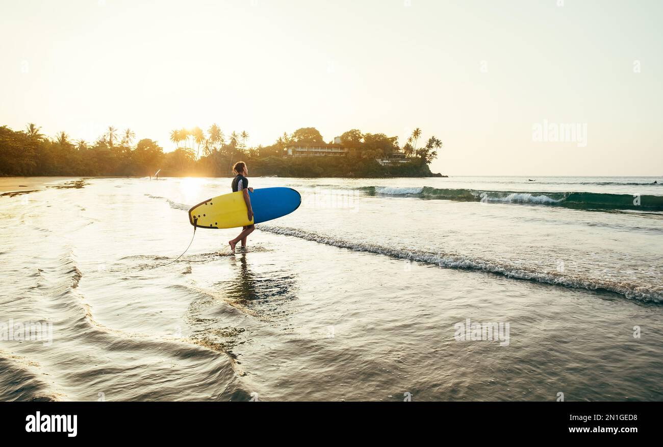 Teen boy with blue and yellow surfboard entering the waves for surfing ...