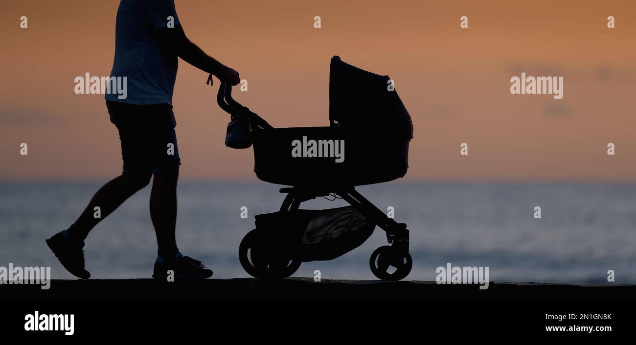 Silhouette of a walking man with a baby stroller at sunset, ocean coast ...