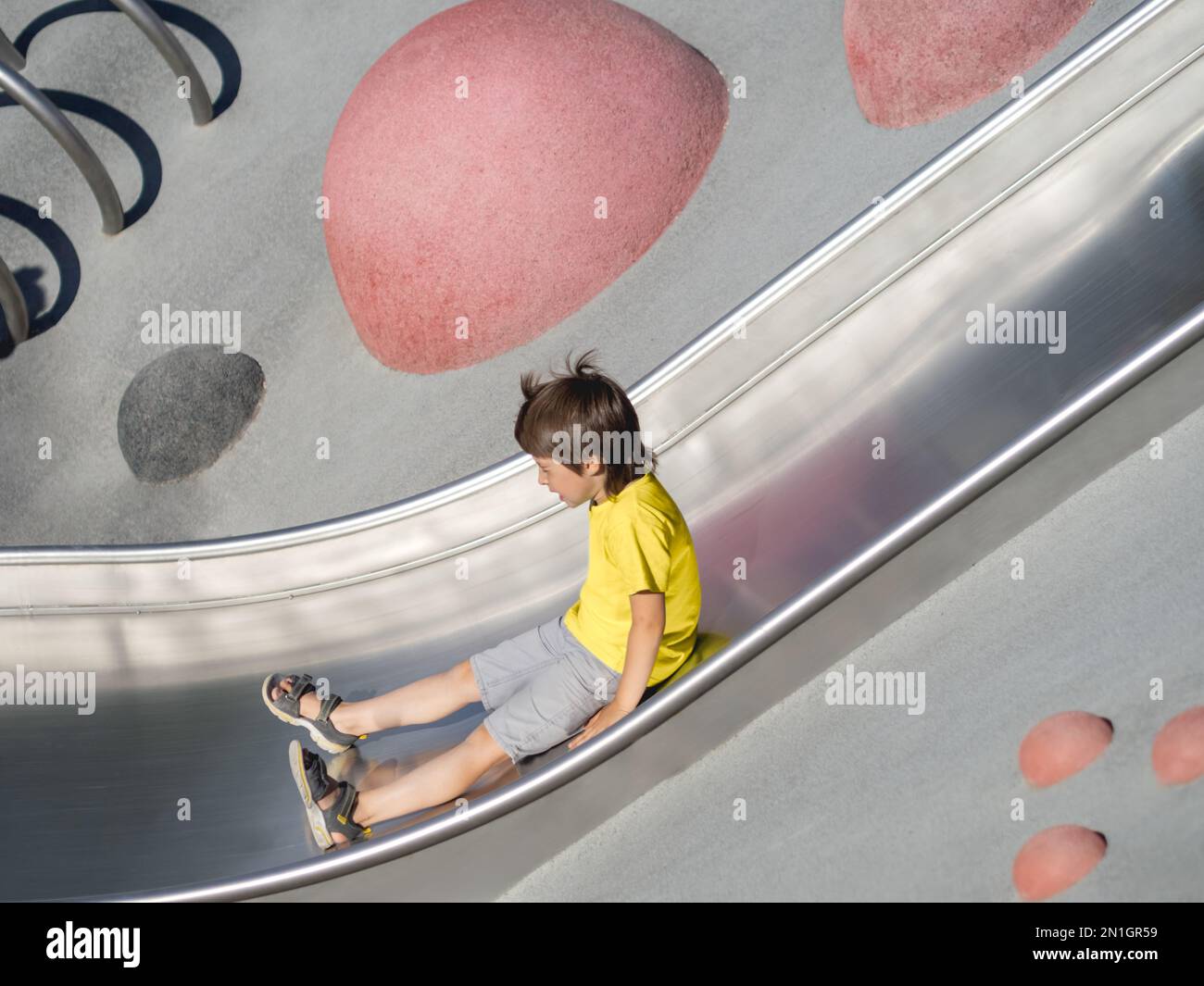 Boy with his eyes closed rides down a metal slide on modern children's ...