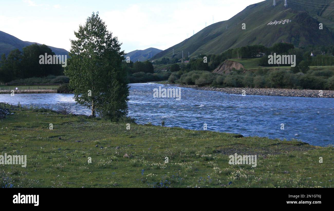 A blue river flowing beside a mountain at a rural landscape Stock Photo ...