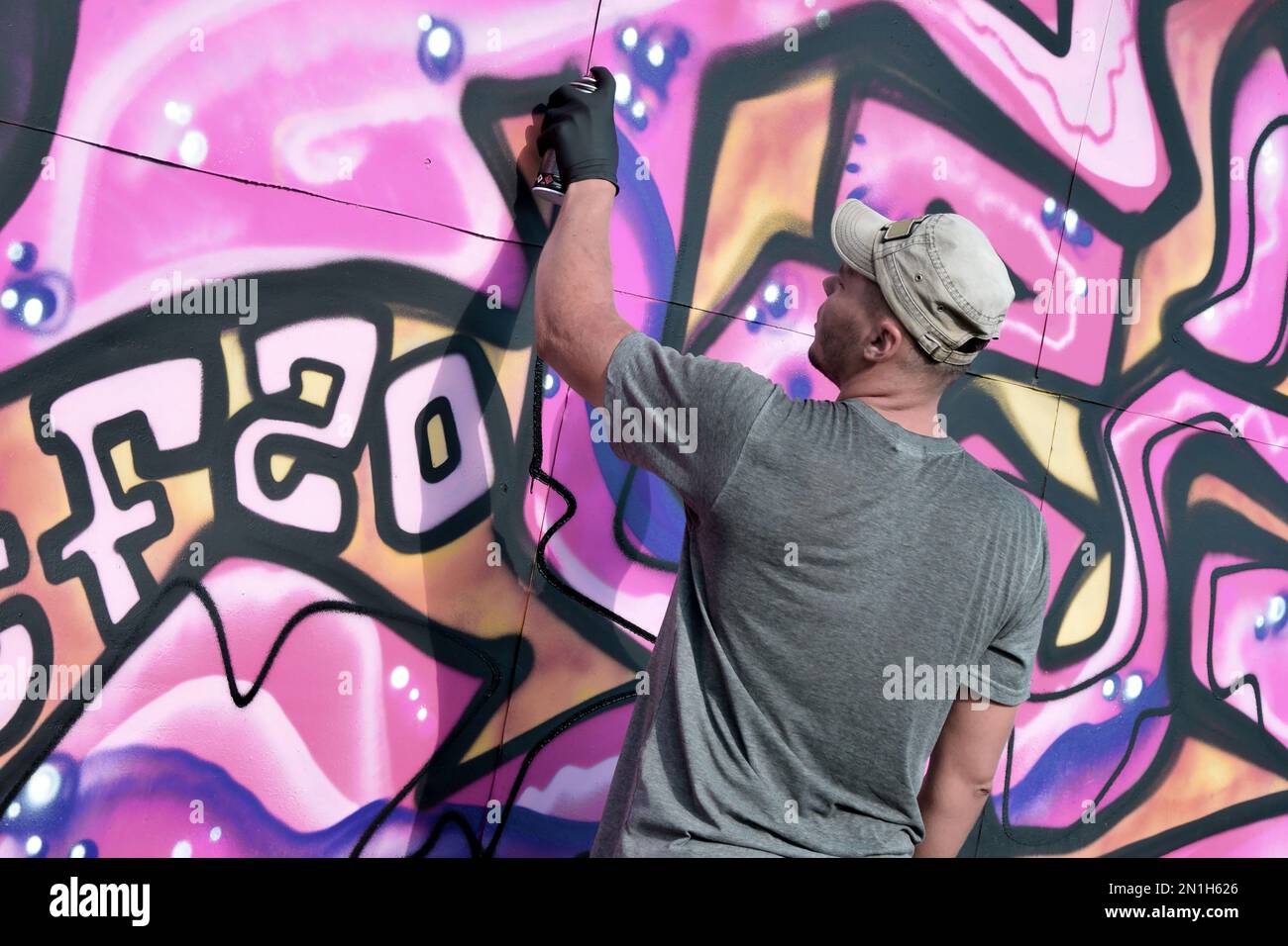 Young caucasian male graffiti artist drawing big street art painting in ...
