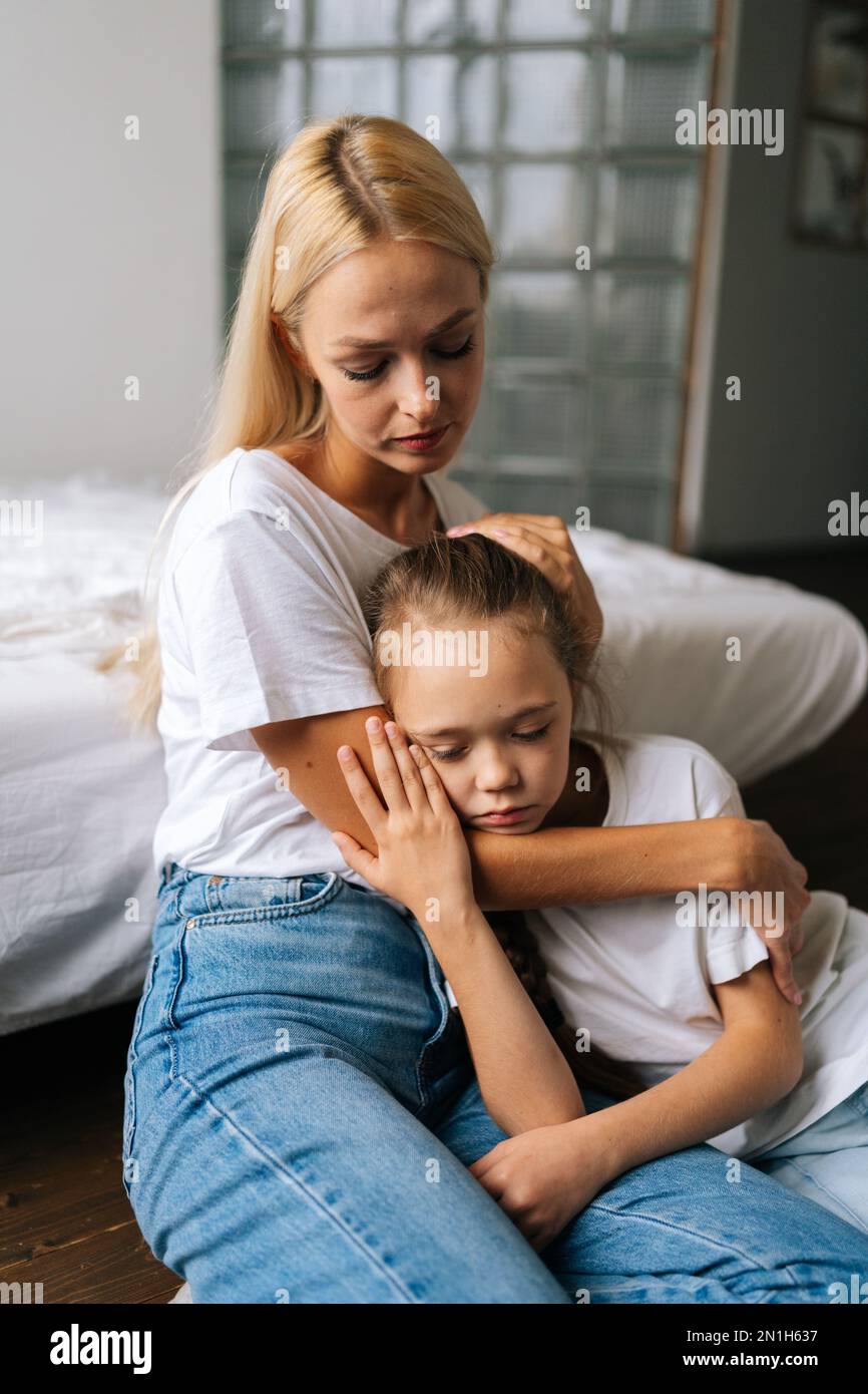 Vertical portrait of loving caring young mother comforting offended sad little daughter lying ...