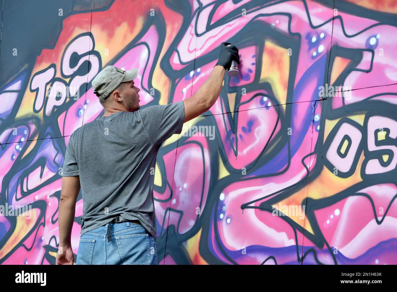 Young caucasian male graffiti artist drawing big street art painting in ...