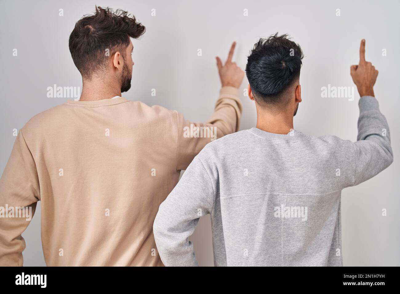 Young homosexual couple standing over white background posing backwards ...