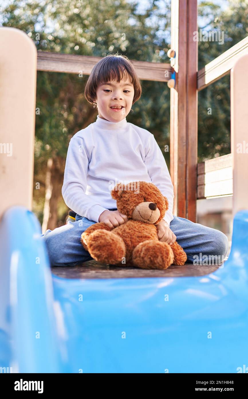 Down syndrome kid smiling confident playing with teddy bear on slide at park Stock Photo - Alamy
