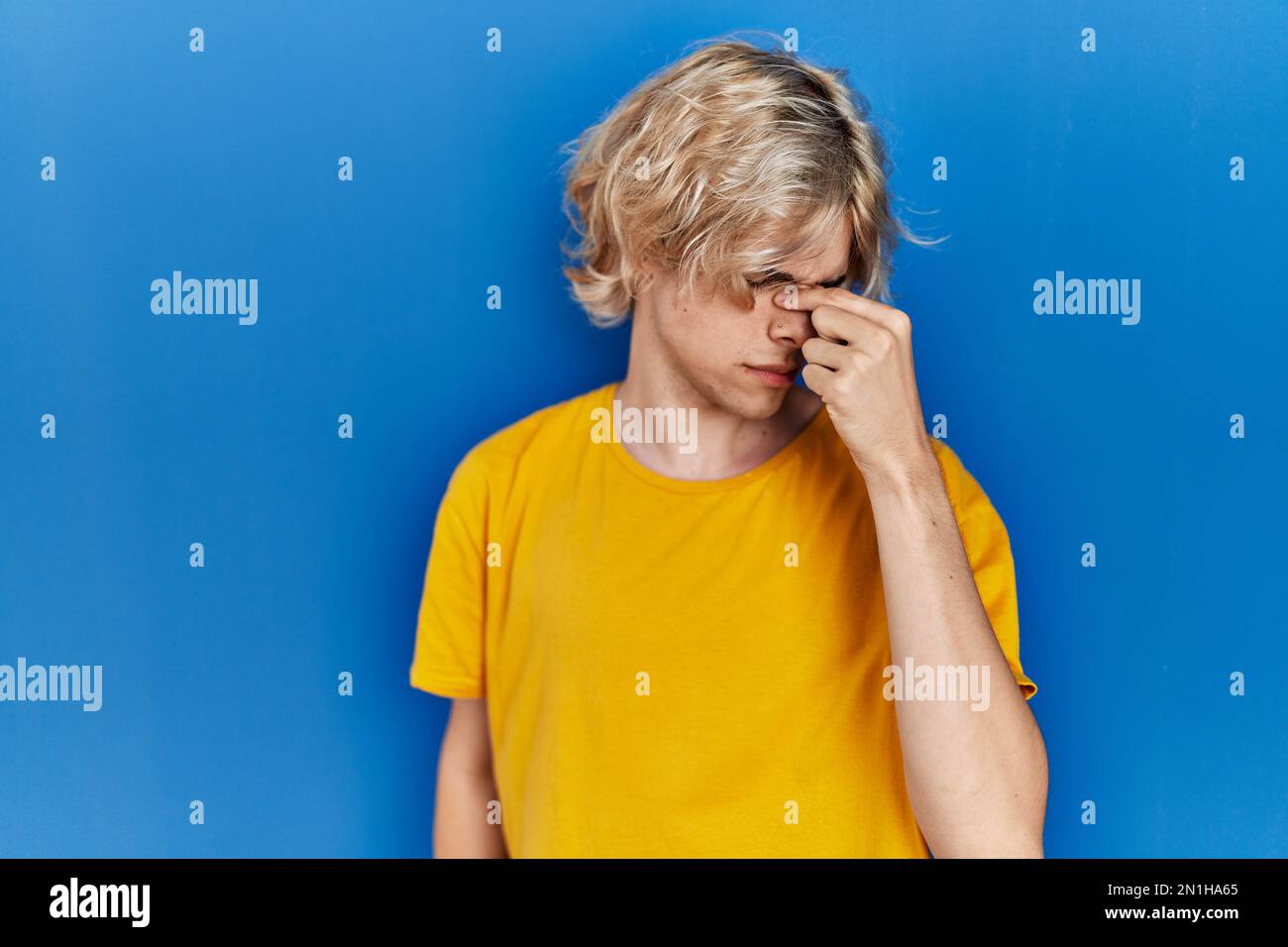 Young modern man standing over blue background tired rubbing nose and ...