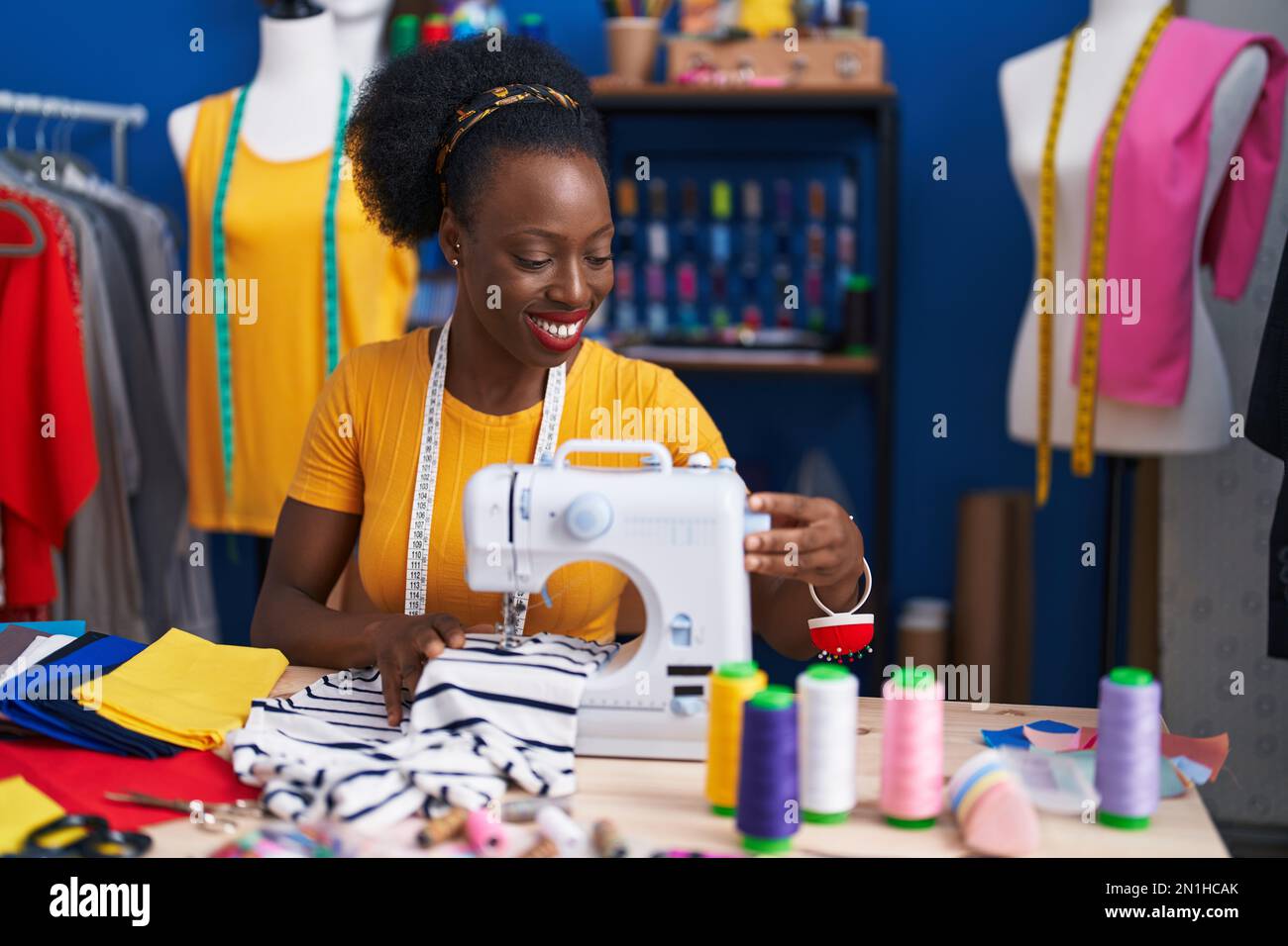 African american woman tailor smiling confident using sewing machine at ...