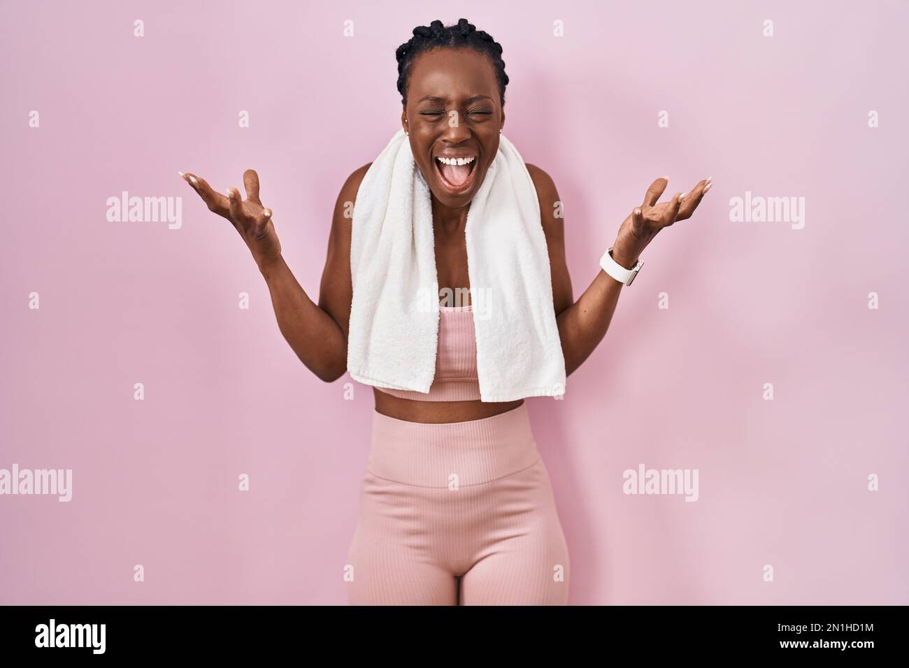 Beautiful black woman wearing sportswear and towel over pink background ...