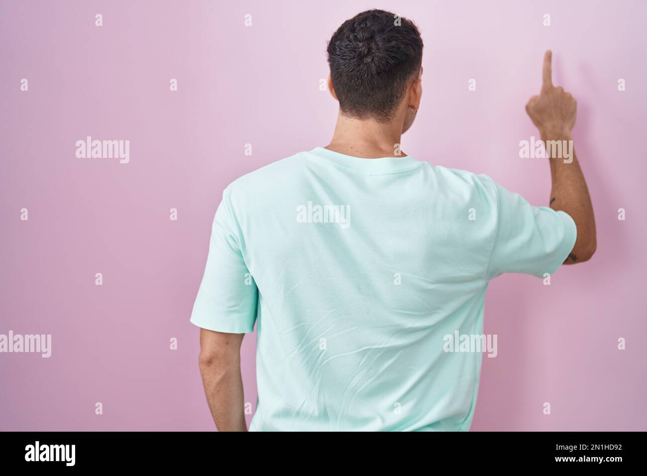 Handsome hispanic man standing over pink background posing backwards ...