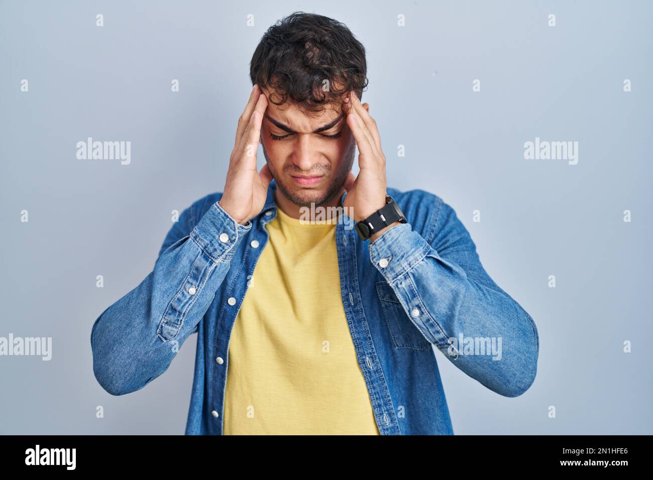 Young hispanic man standing over blue background with hand on head ...