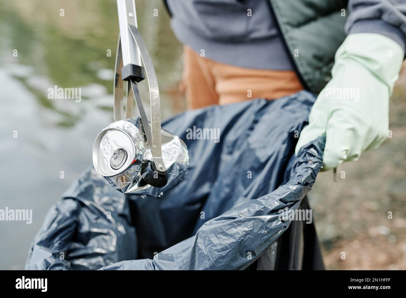 Closeup image of city park worker collecting garbage with special stick ...