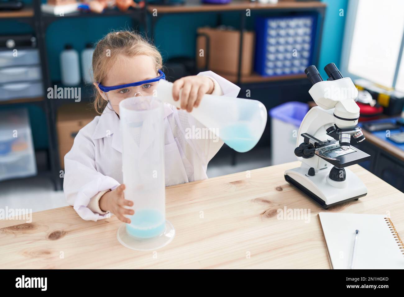 Adorable blonde girl student pouring liquid on test tube at laboratory ...