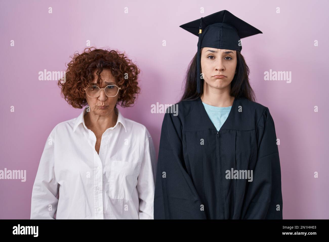 Hispanic mother and daughter wearing graduation cap and ceremony robe ...