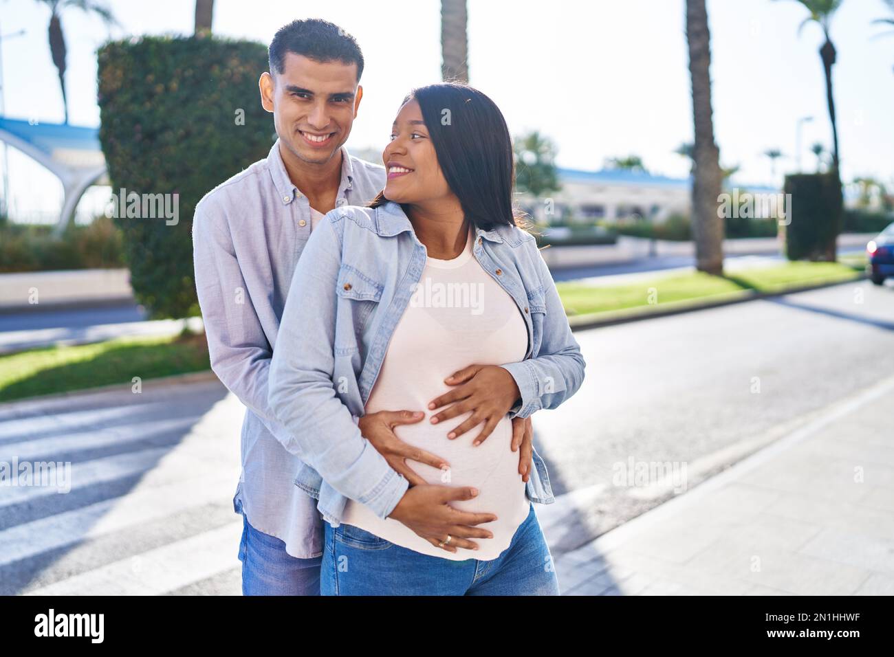 Young latin couple expecting baby hugging each other standing at street Stock Photo - Alamy