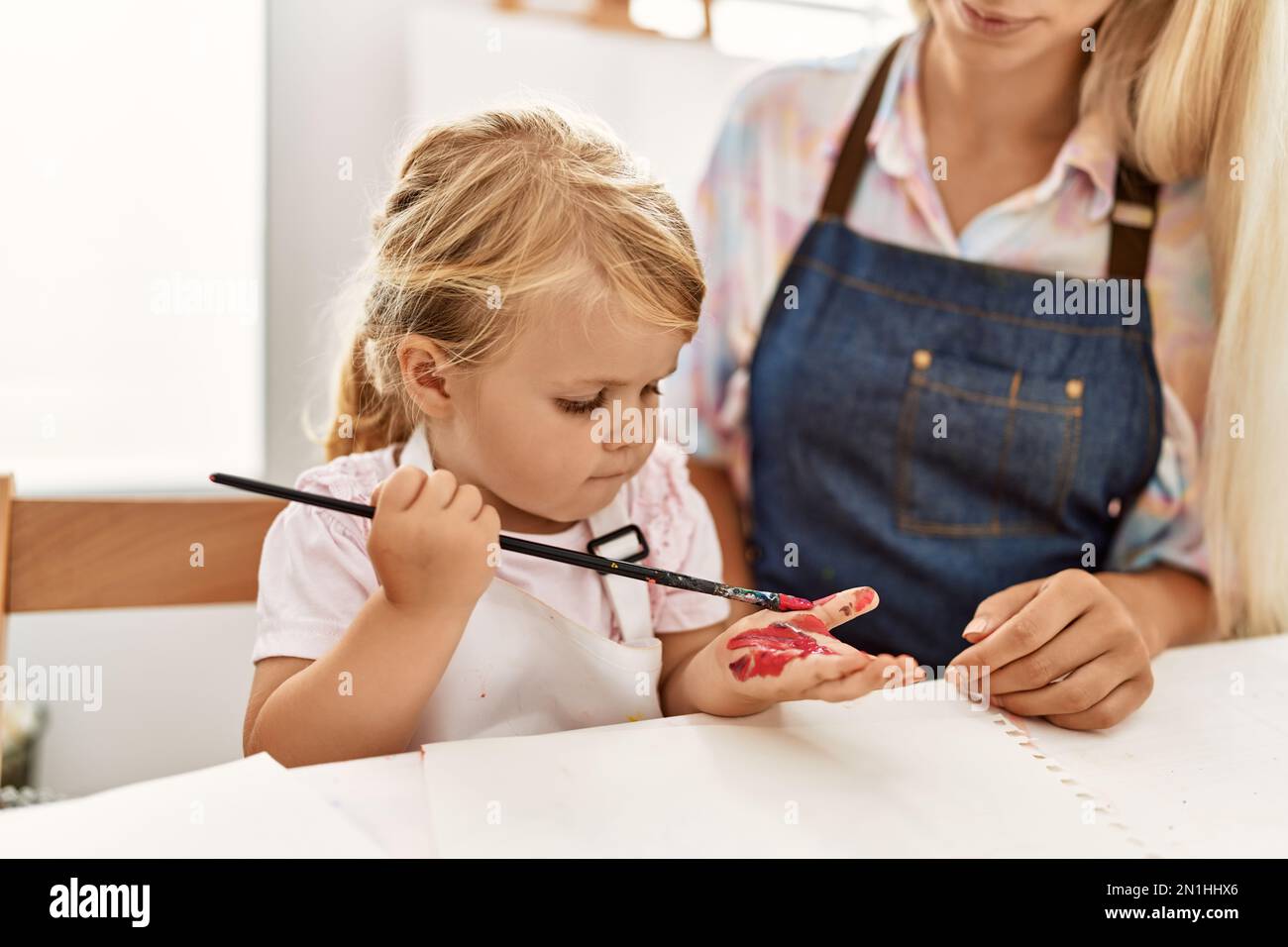 Mother and daughter smiling confident painting palm hands at art studio ...