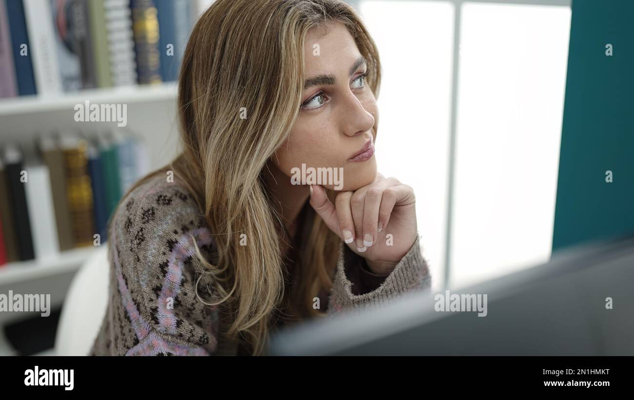 Young blonde woman student using computer studying with doubt ...