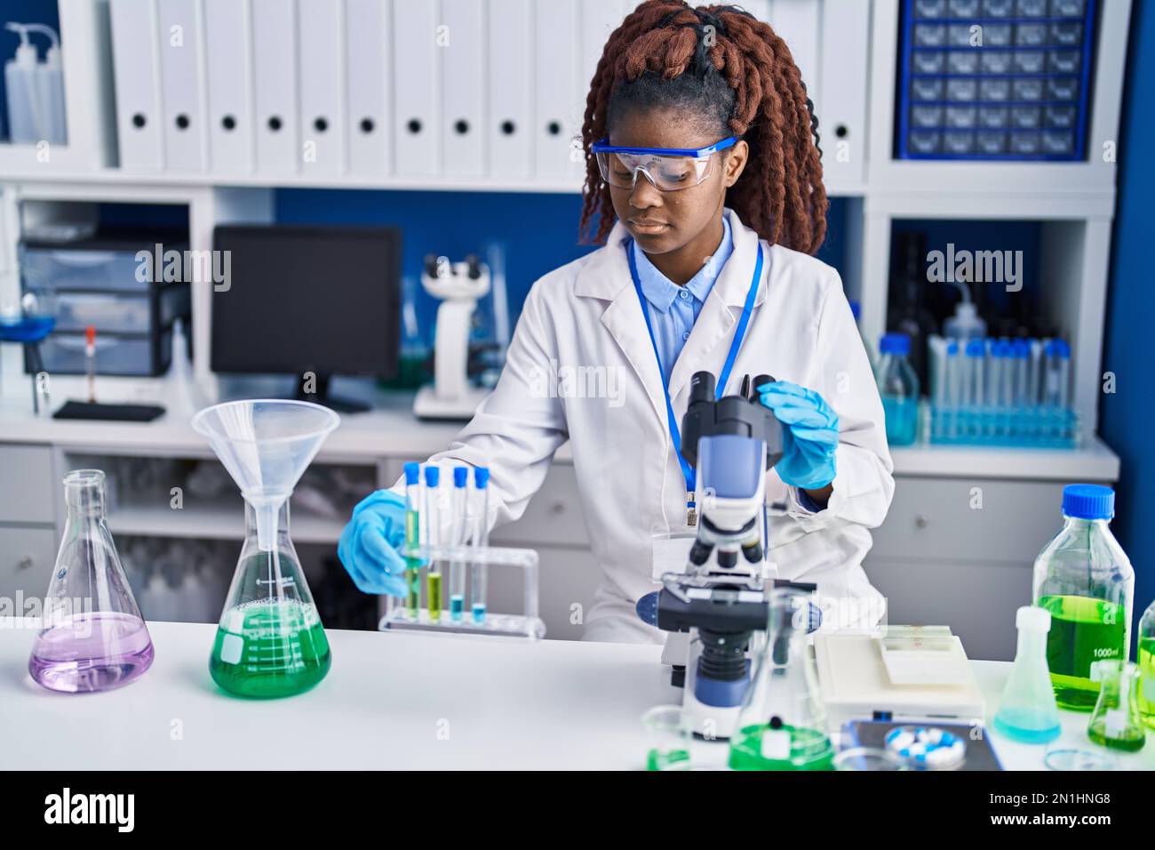 African american woman scientist using microscope holding test tubes at ...