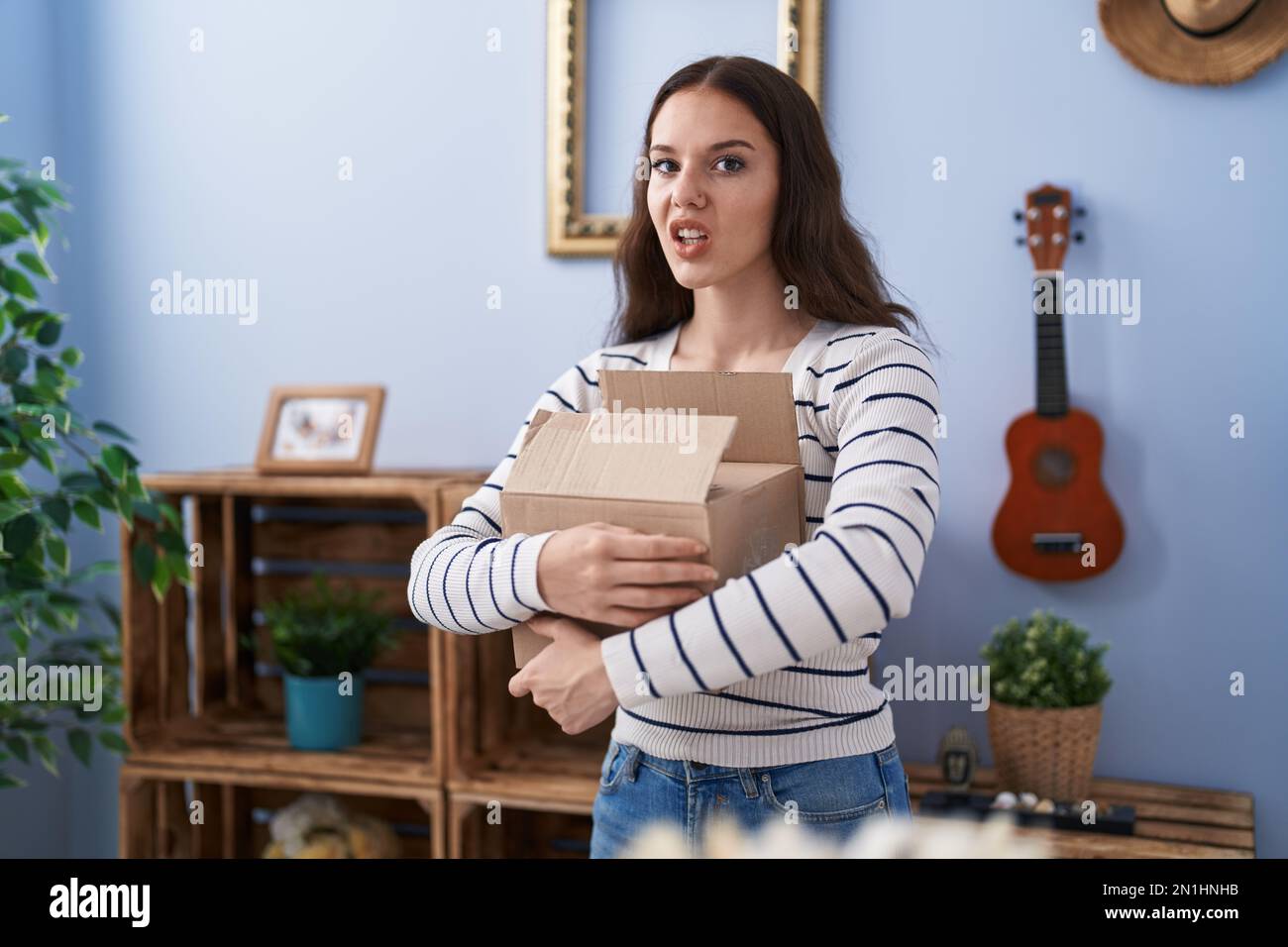 Young hispanic girl opening cardboard box clueless and confused ...