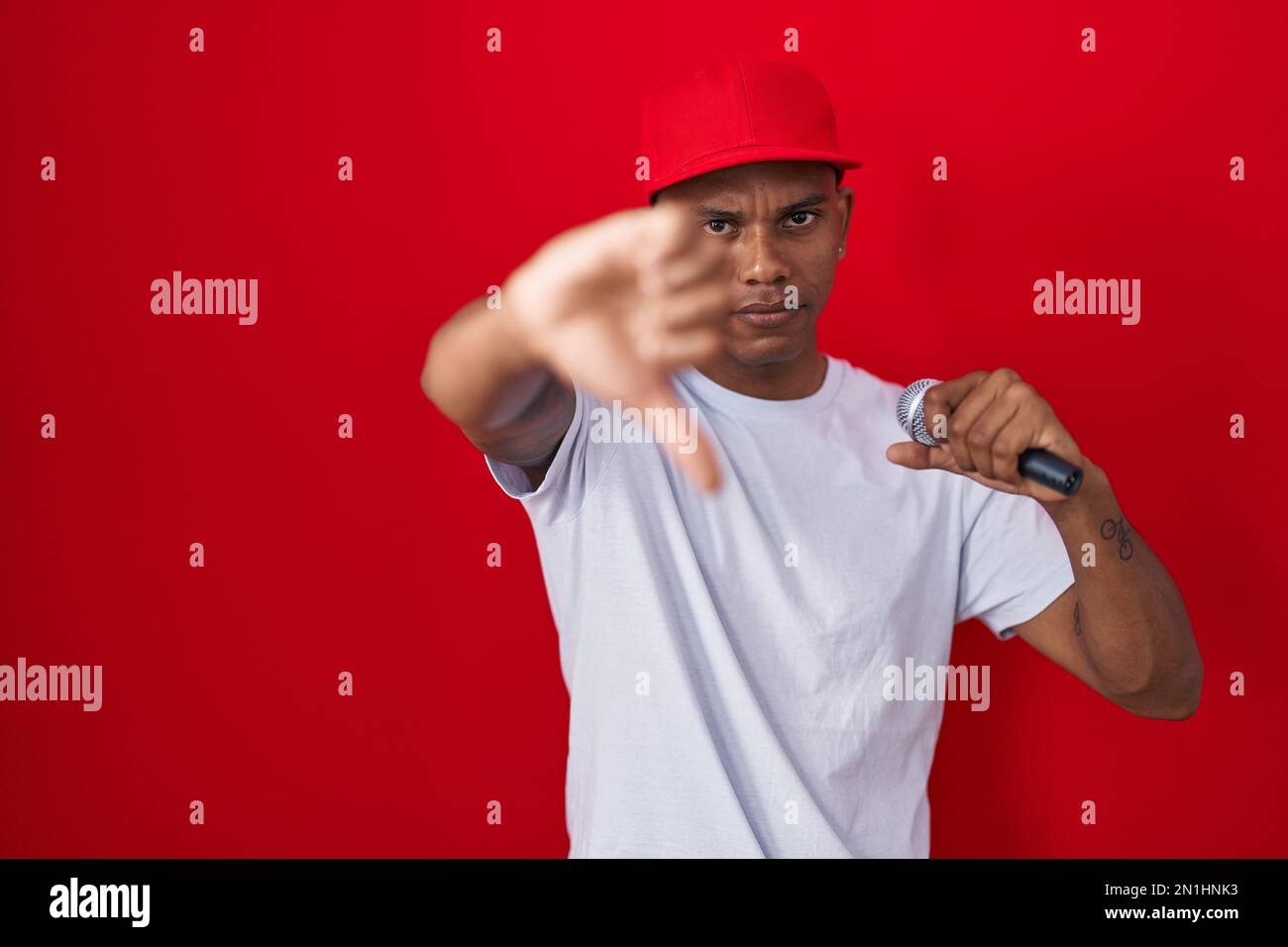 Young hispanic man singing song using microphone with angry face ...