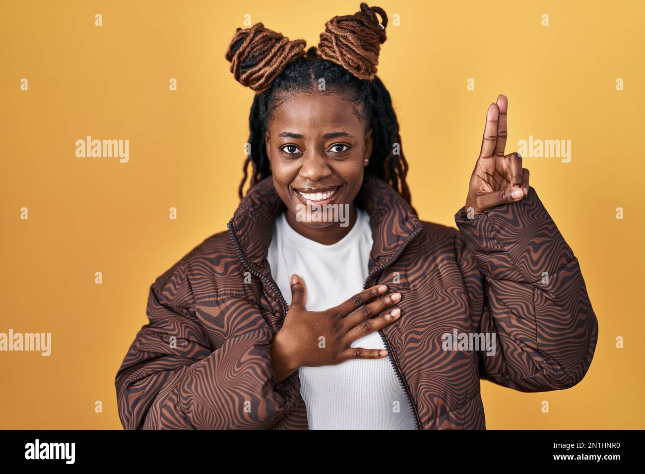 African woman with braided hair standing over yellow background smiling ...