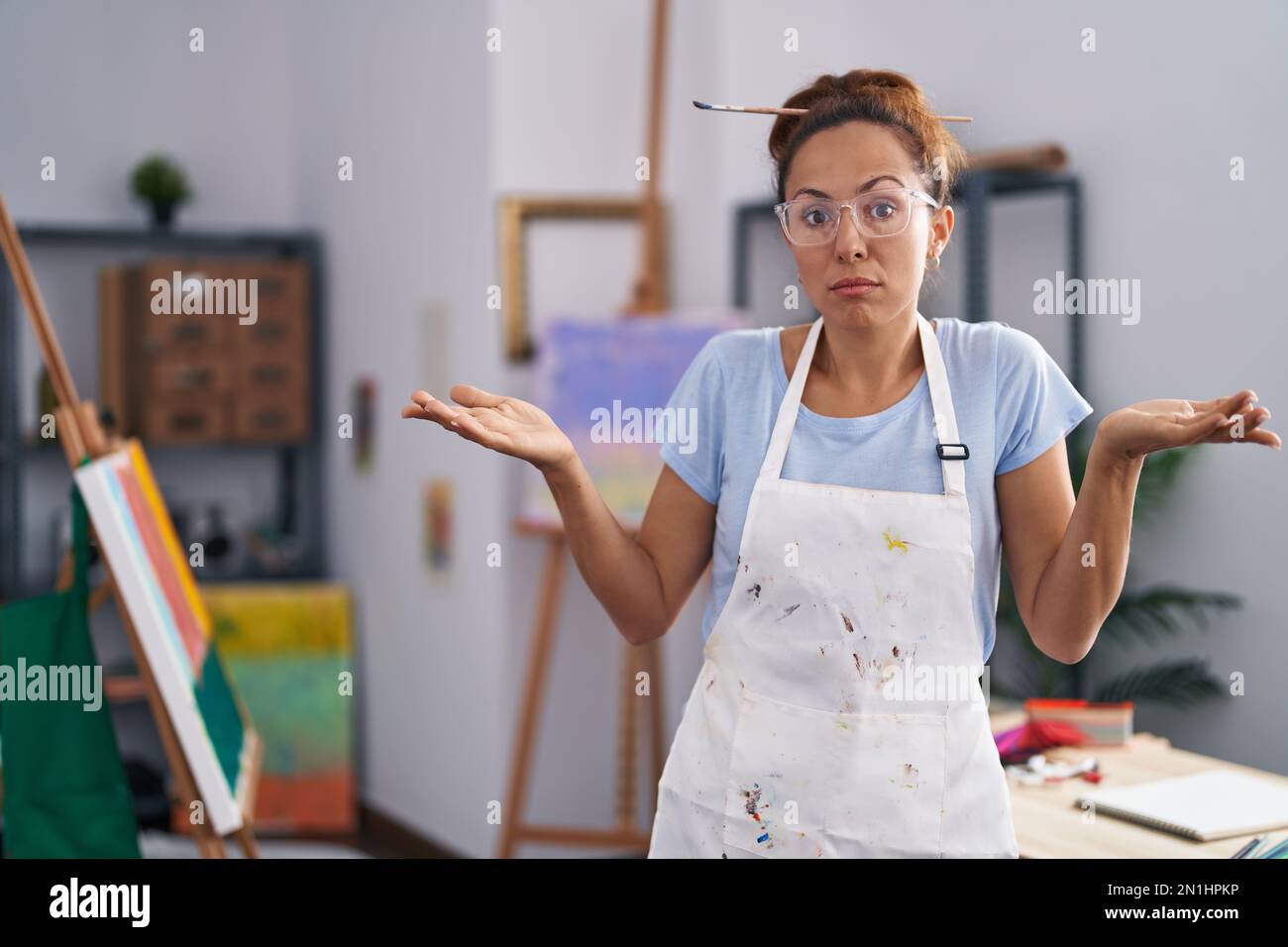 Brunette woman painting at art studio clueless and confused expression ...