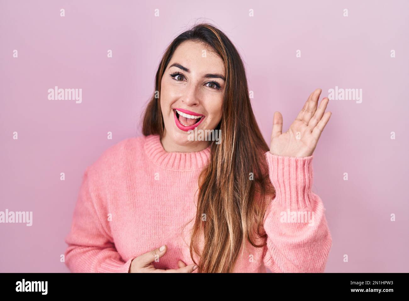 Young hispanic woman standing over pink background waiving saying hello ...