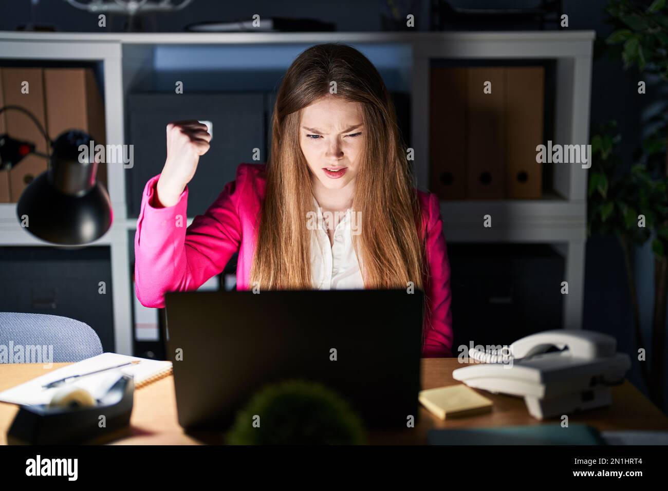 Young caucasian woman working at the office at night angry and mad ...