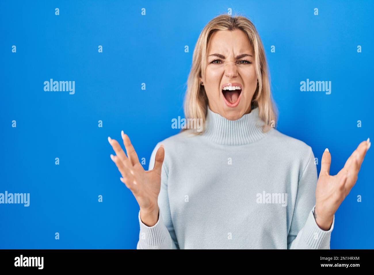 Young caucasian woman standing over blue background crazy and mad ...