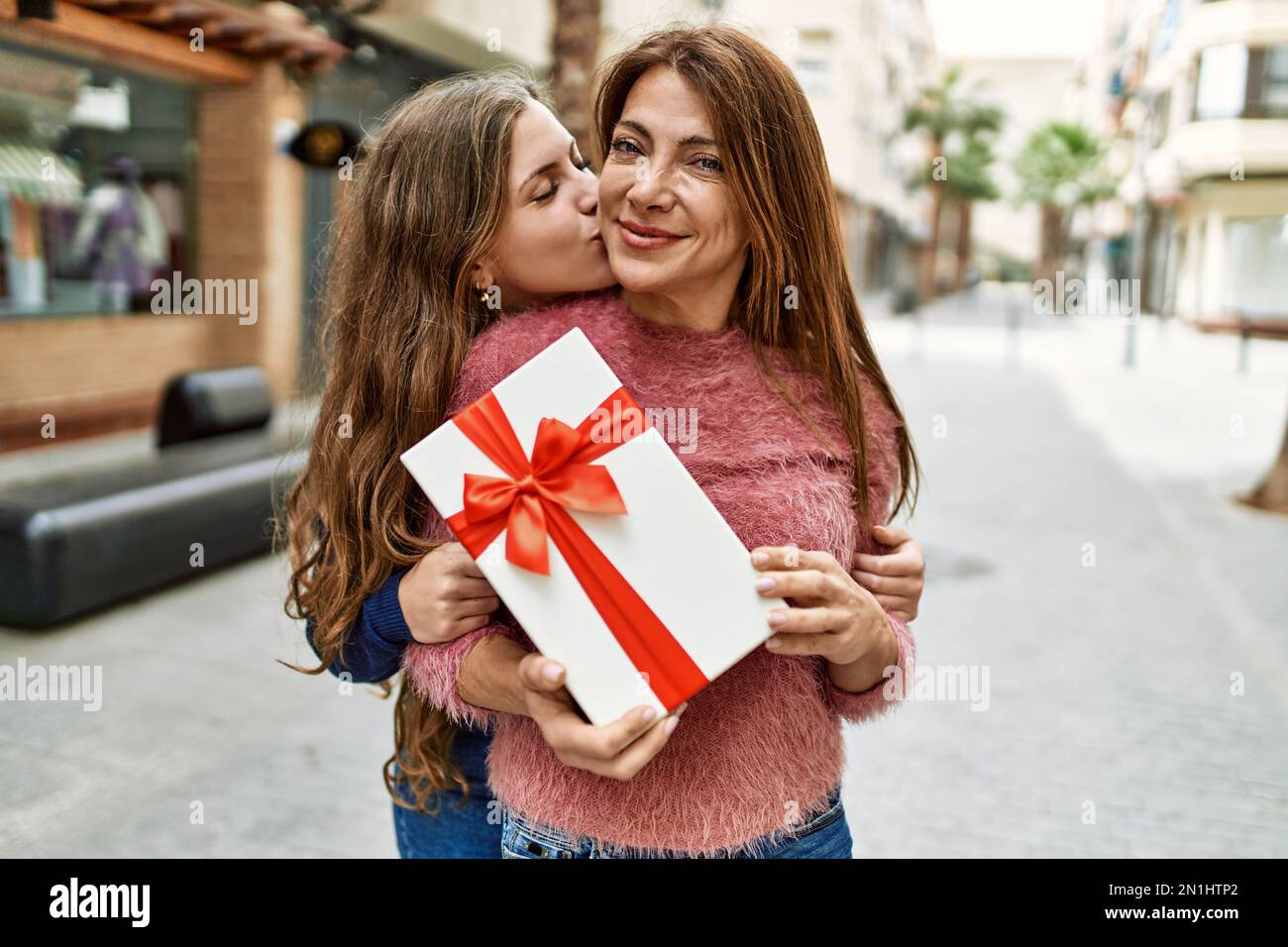 Mother and daughter hugging each other and kissing holding birthday gift at street Stock Photo ...