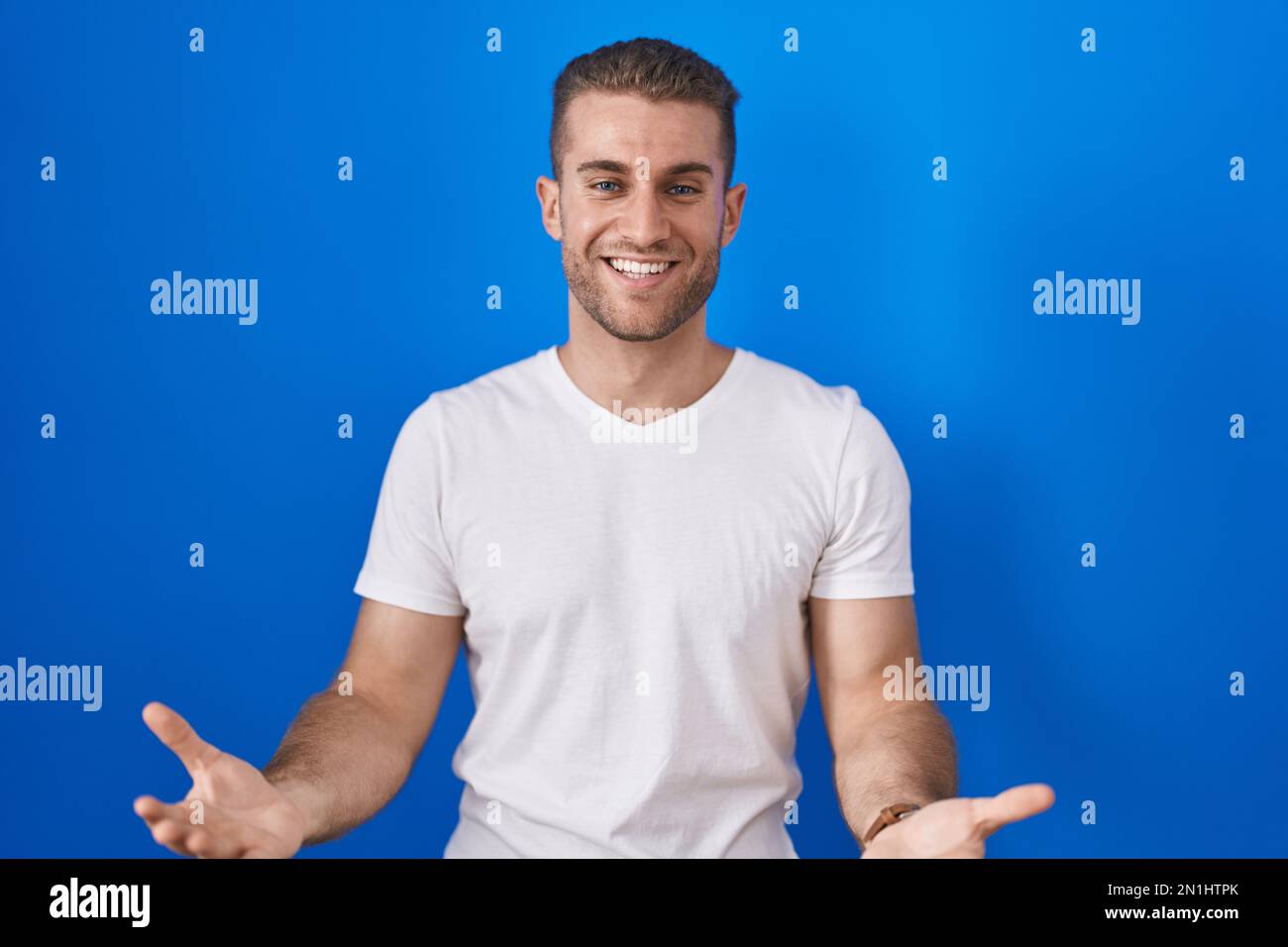 Young caucasian man standing over blue background smiling cheerful with ...