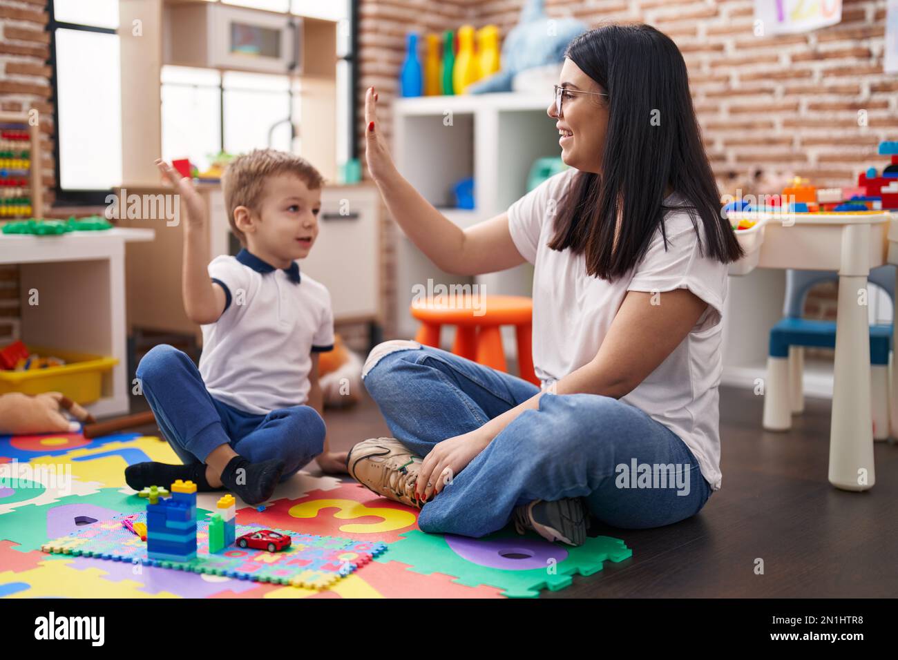 Teacher and toddler sitting on floor high five with hands raised up at ...