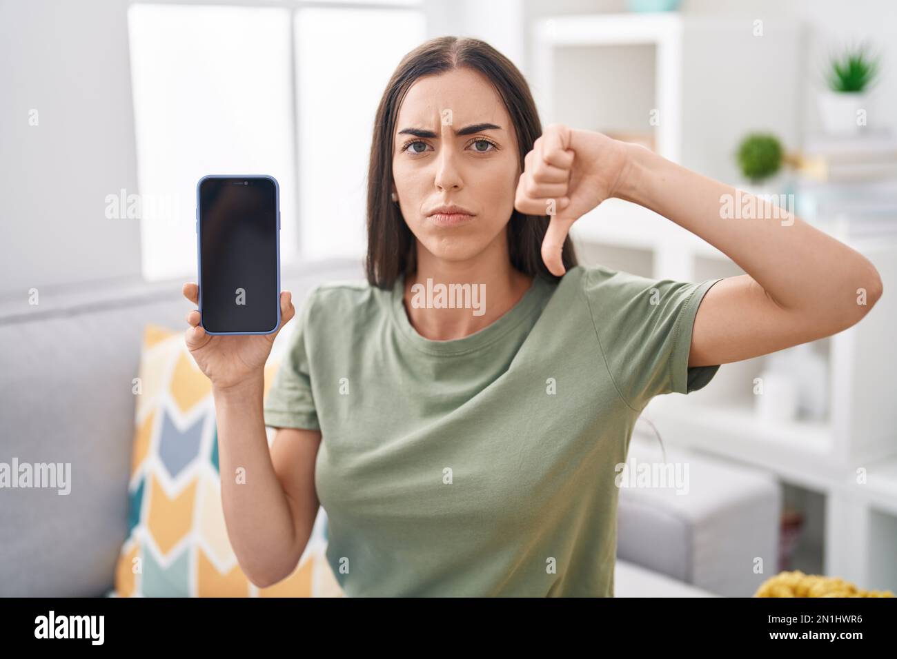Young brunette woman holding smartphone showing blank screen with angry ...