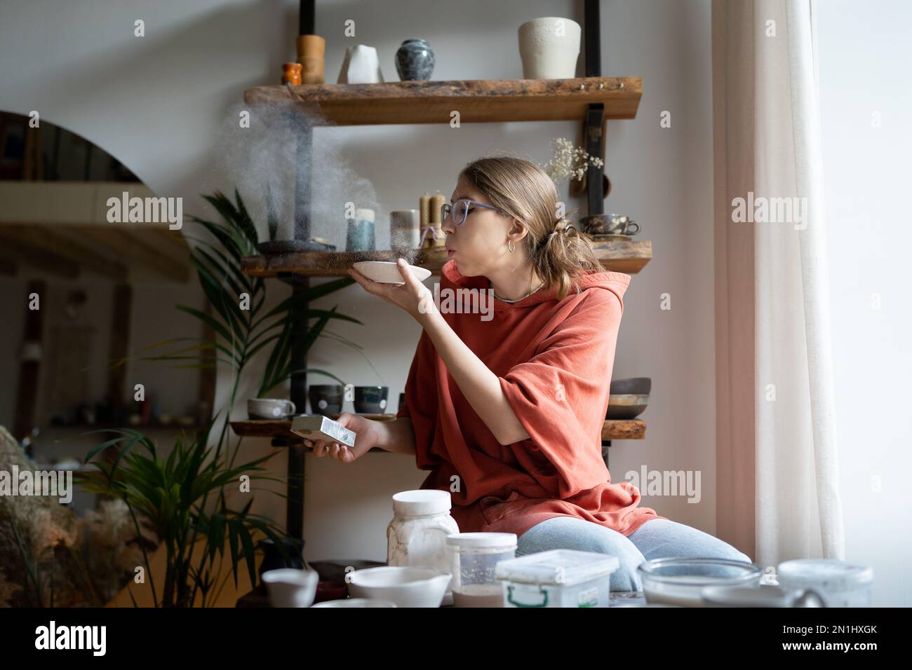 Lonely self-sufficient woman sculptor blowing dust particles off plate ...