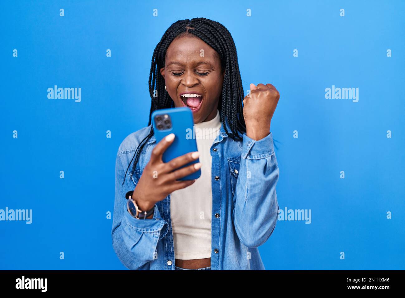 African woman with braids using smartphone typing message annoyed and ...