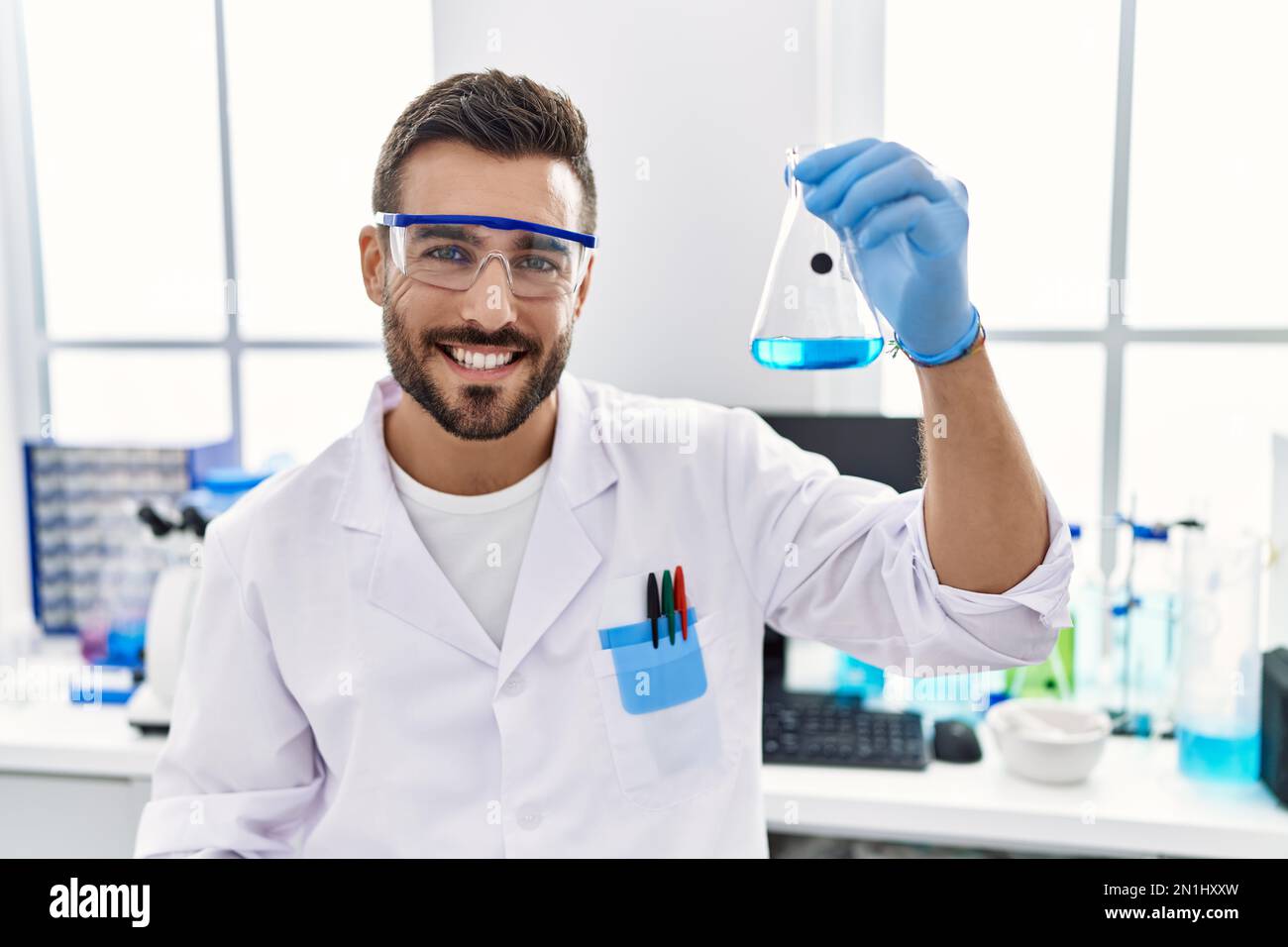 Young hispanic man wearing scientist uniform holding test tube at ...