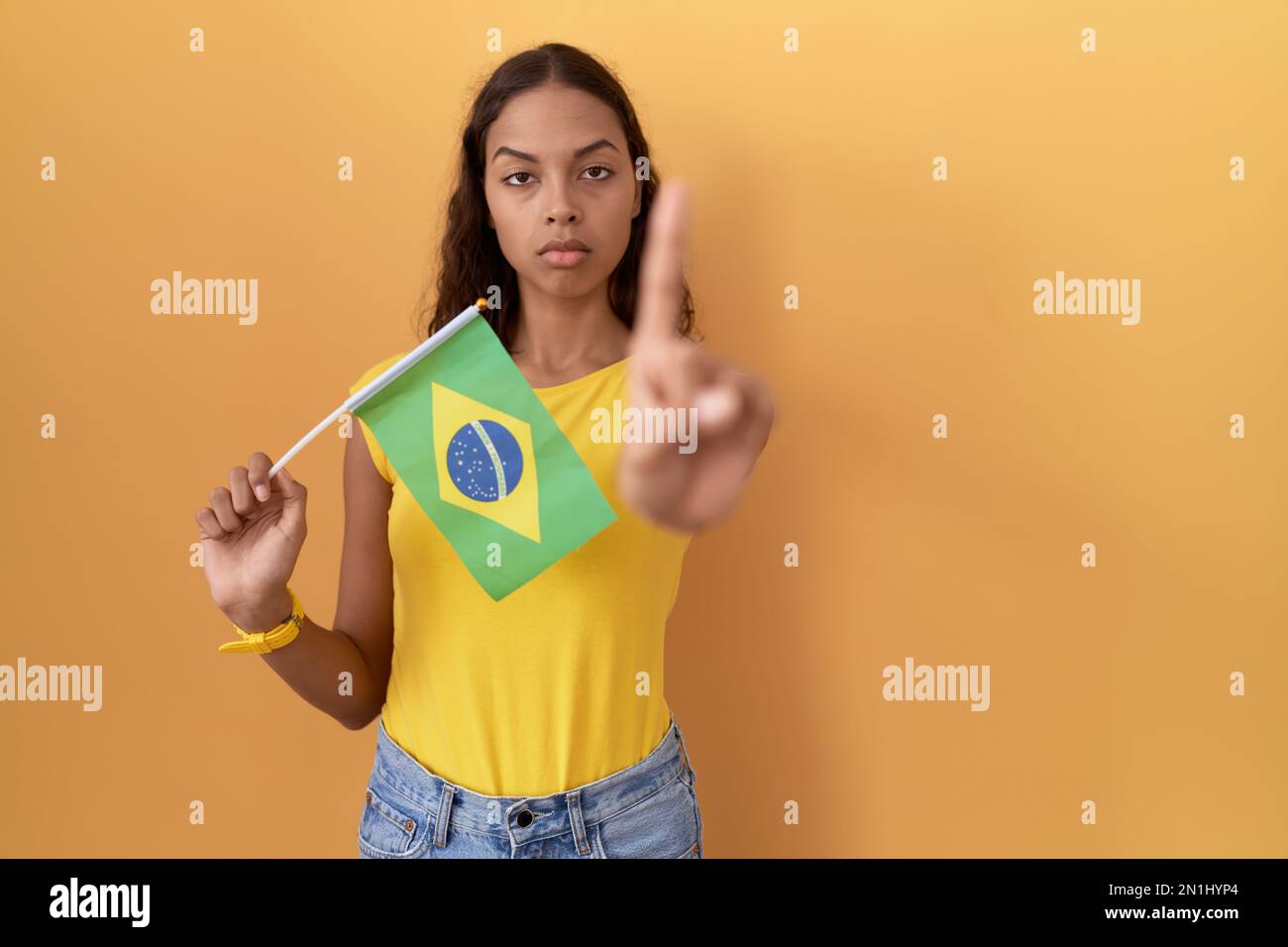 Young hispanic woman holding brazil flag pointing with finger up and ...