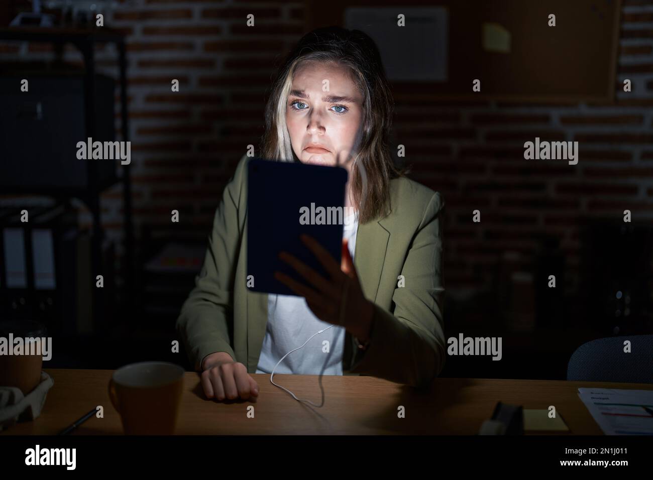 Blonde caucasian woman working at the office at night depressed and ...