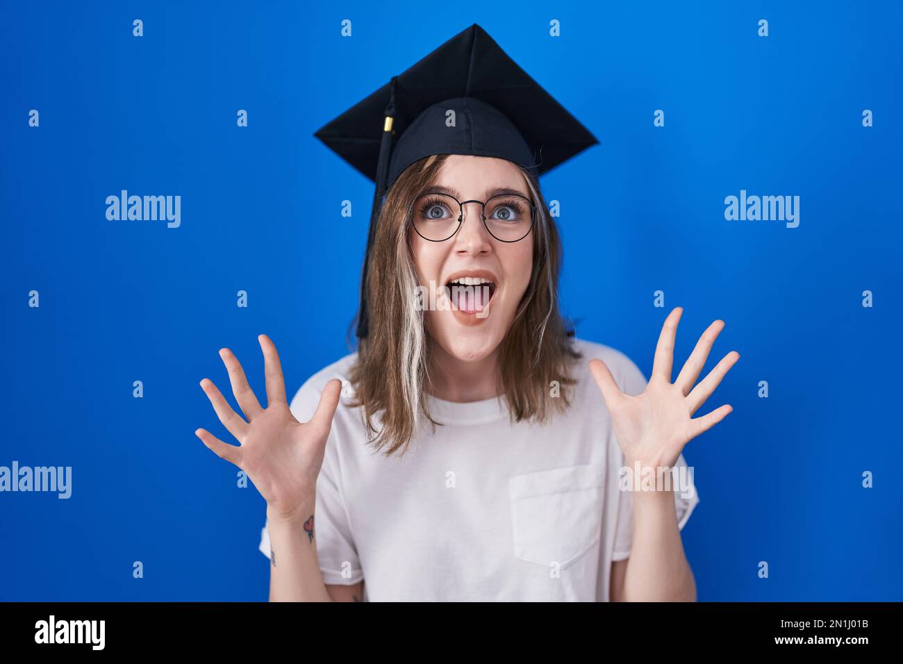 Blonde caucasian woman wearing graduation cap crazy and mad shouting ...