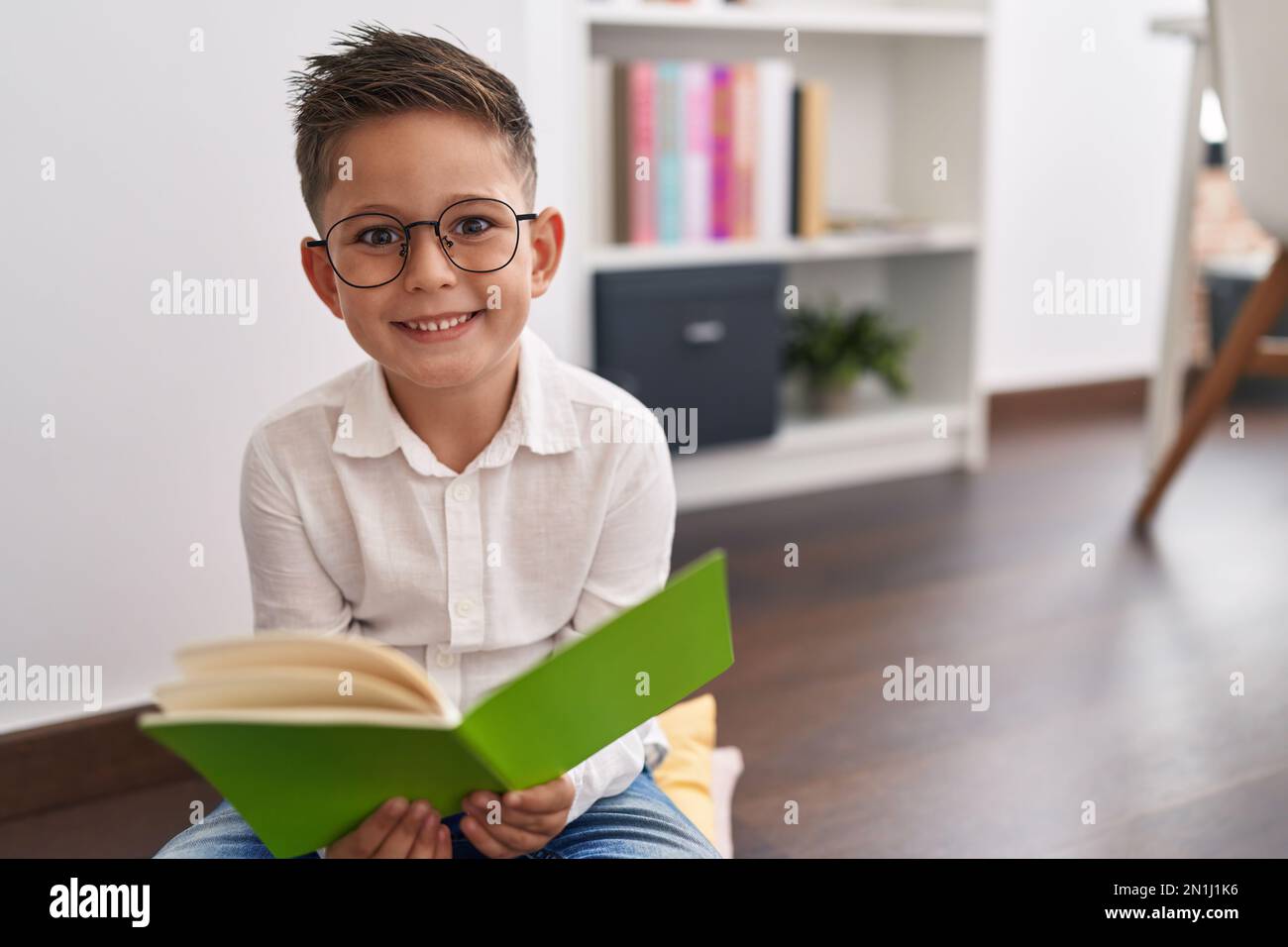 Adorable hispanic boy student smiling confident reading book at library ...