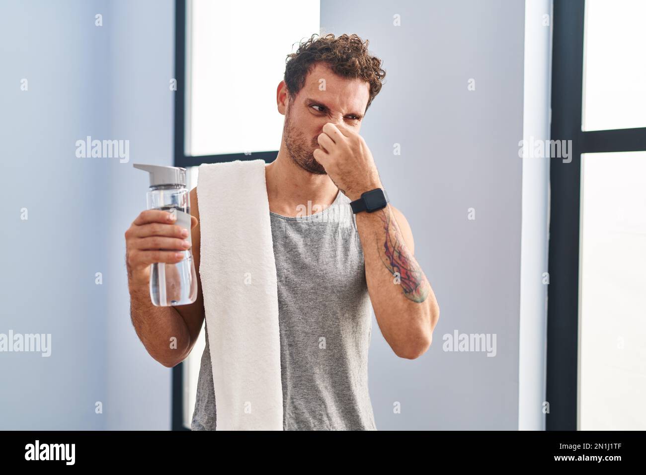 Young hispanic man wearing sportswear drinking water smelling something ...