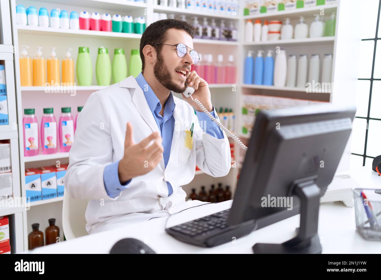 Young hispanic man pharmacist talking on telephone using computer at ...
