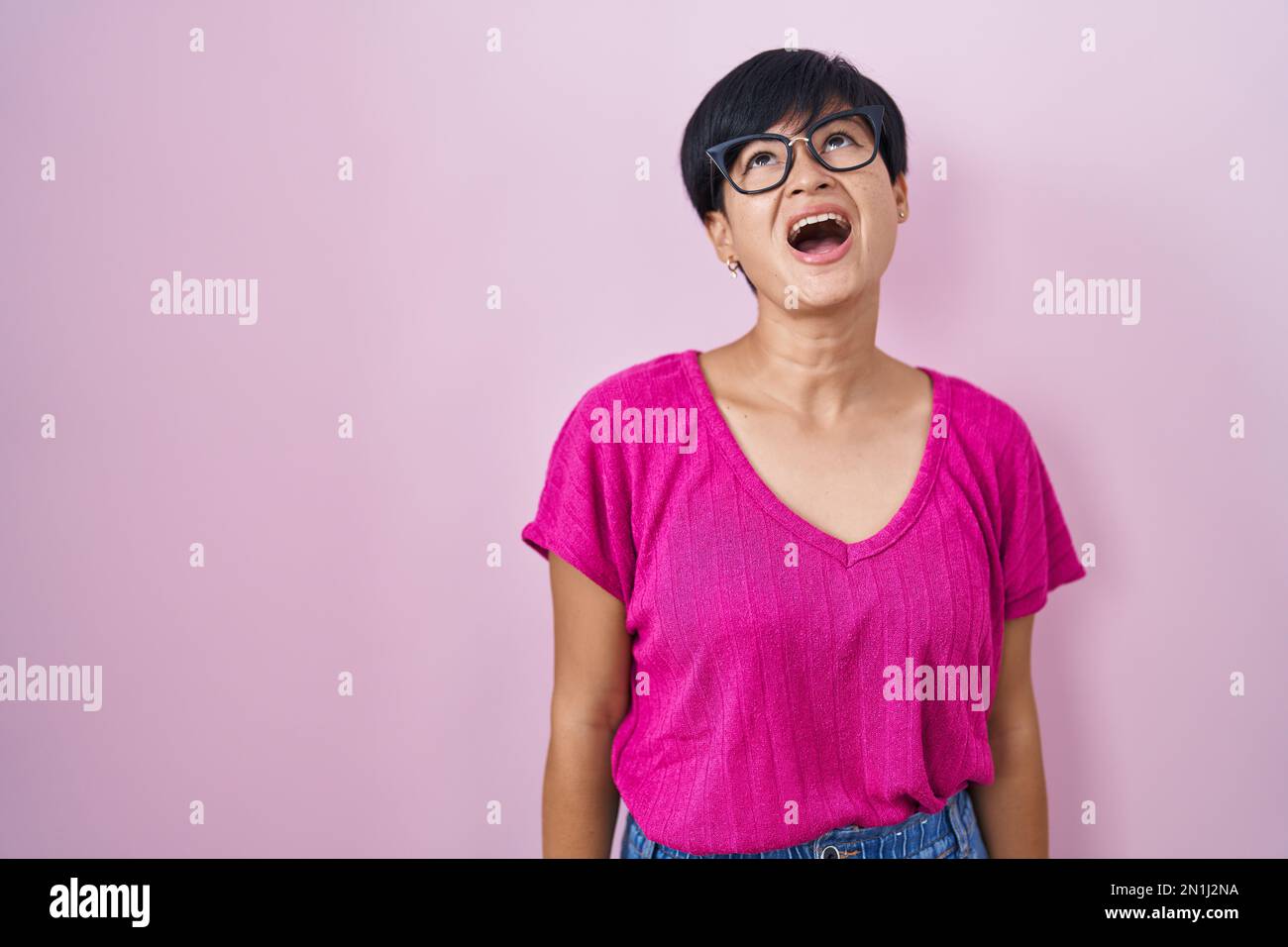 Young asian woman with short hair standing over pink background angry ...