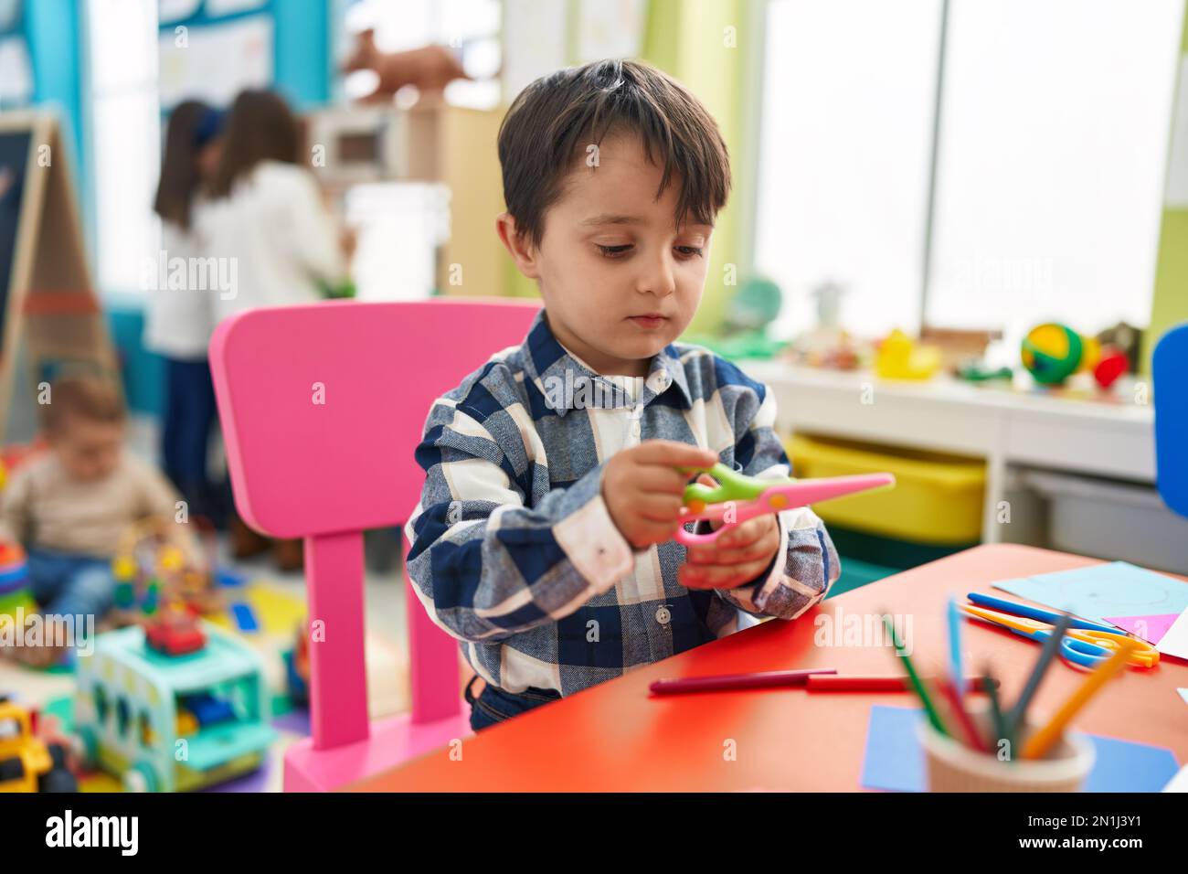 Adorable hispanic boy student holding scissors at kindergarten Stock ...