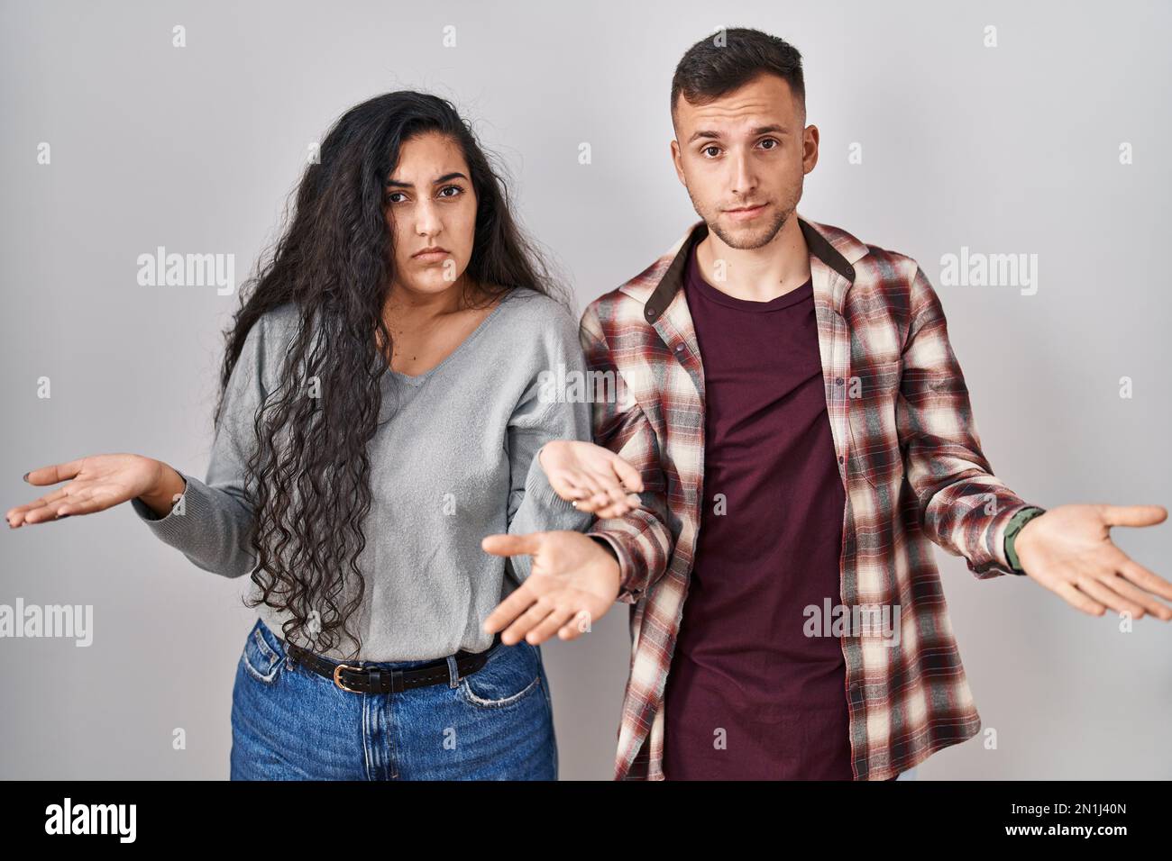 Young hispanic couple standing over white background clueless and ...