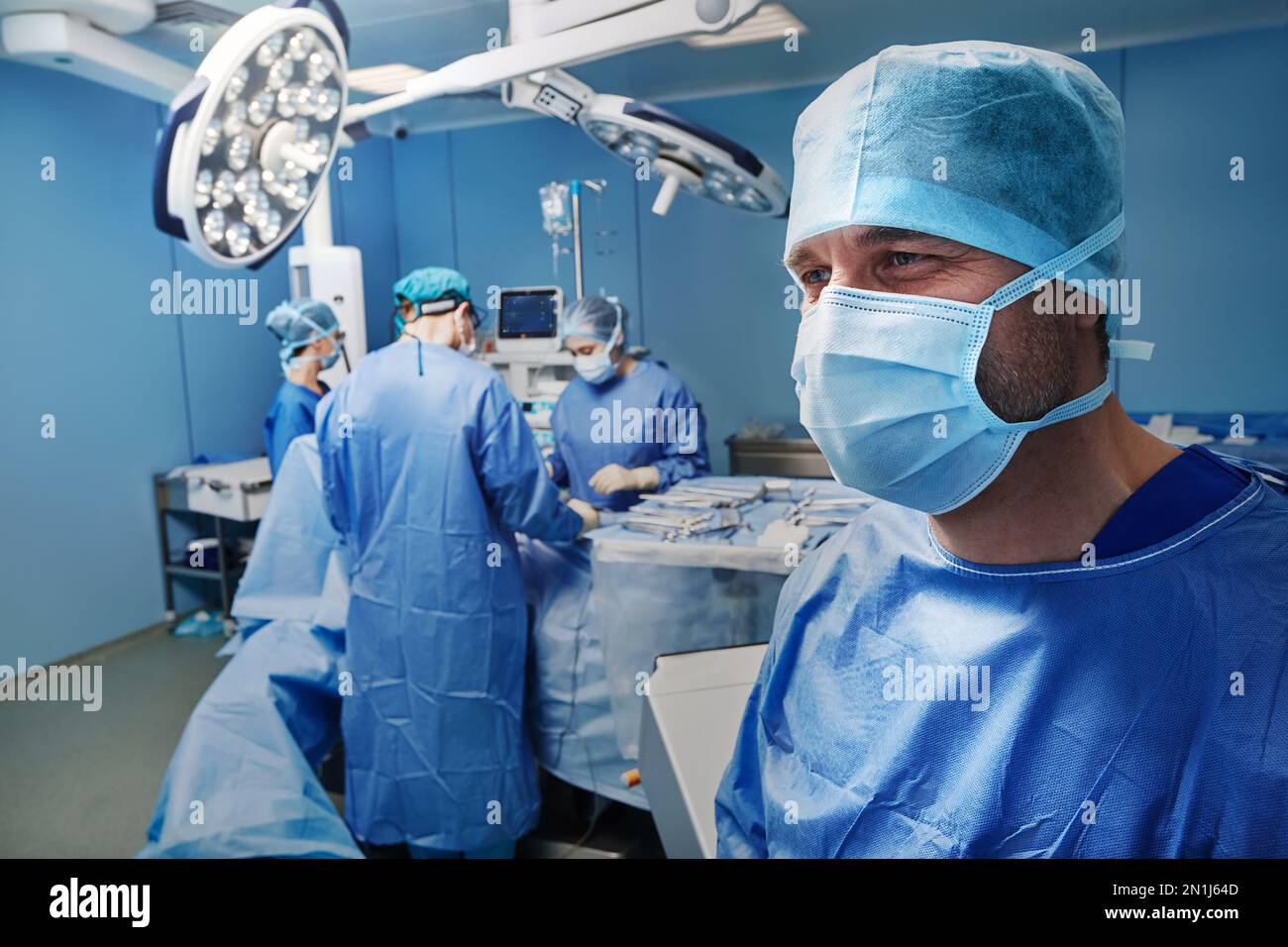 Portrait of male surgeon standing in operating room while colleagues ...
