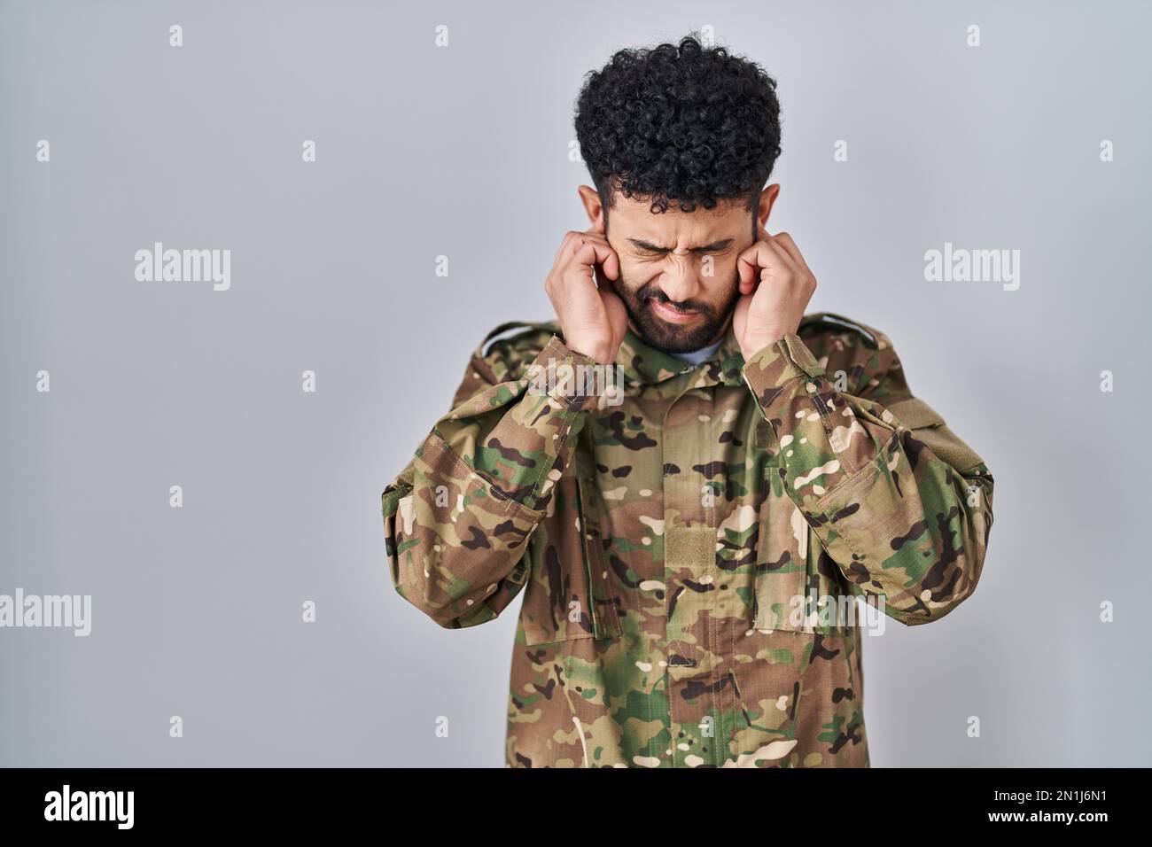 Arab man wearing camouflage army uniform covering ears with fingers ...