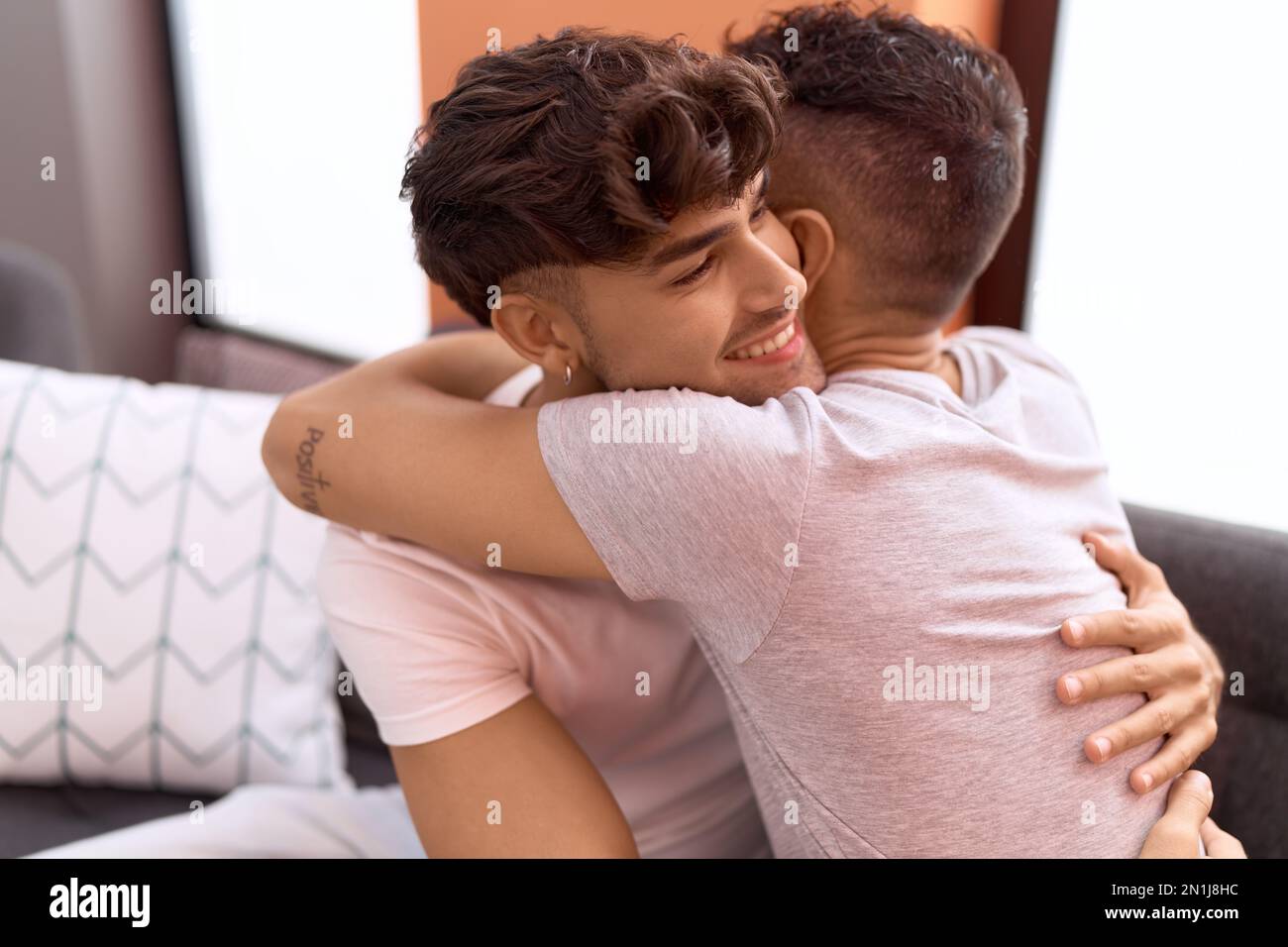 Two hispanic men couple hugging each other sitting on sofa at home ...