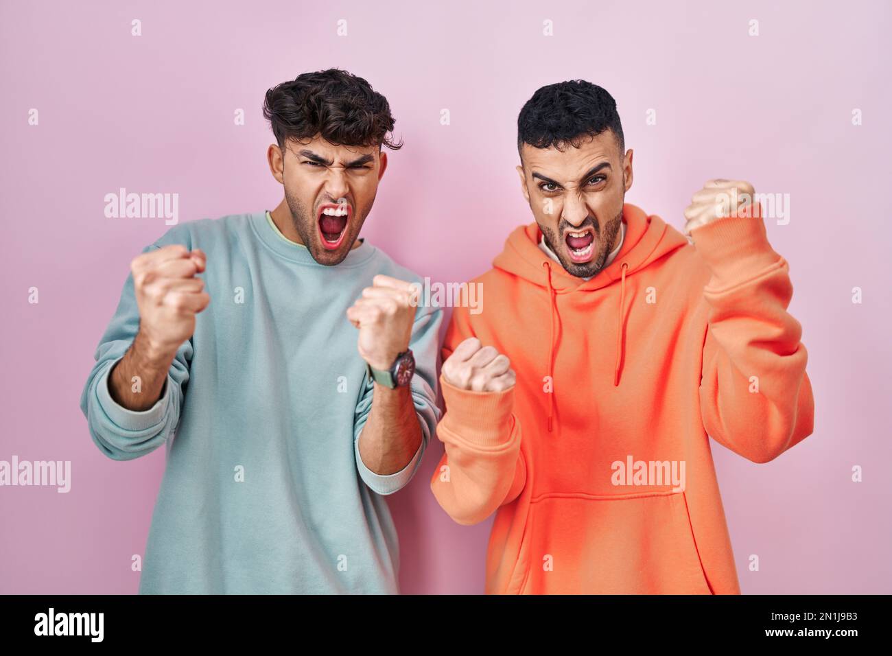 Young hispanic gay couple standing over pink background angry and mad ...