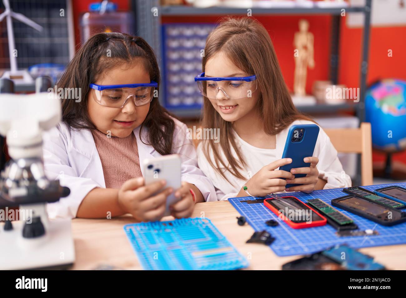 Two kids students using smartphones standing at laboratory classroom ...