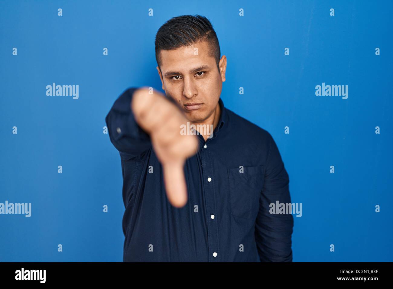 Hispanic young man standing over blue background looking unhappy and ...